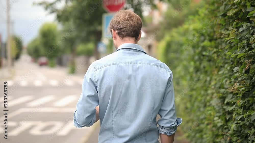 back view of a walking man texting on his phone and turns to say hello ...