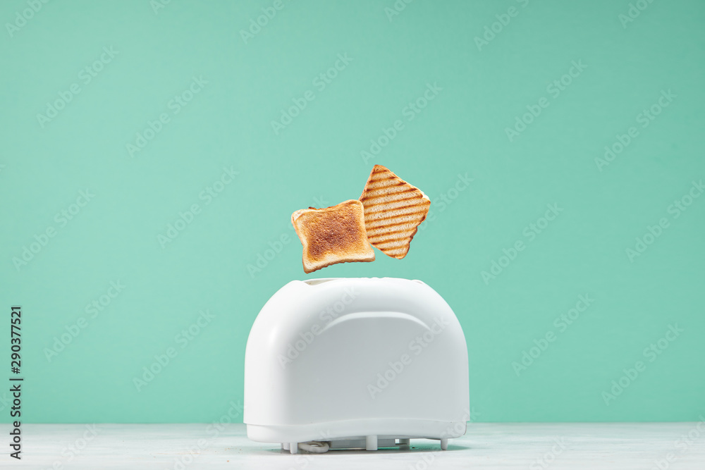 Roasted toast bread popping up of toaster with green wall, front view ...