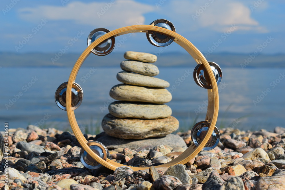 Musical instrument a tambourine and a pyramid of stones on the bank of ...