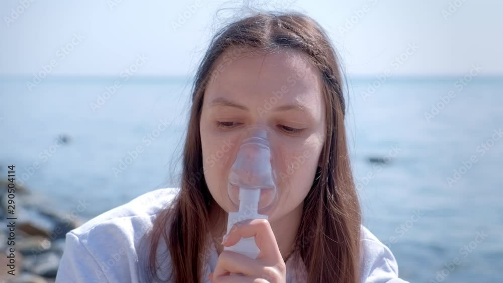Young sick woman use nebulizer on seaside. Inhaling inhaler mask ...