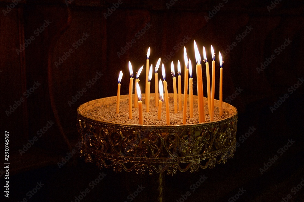 Light from lit candles in a candelabra stand filled with sand and soil ...