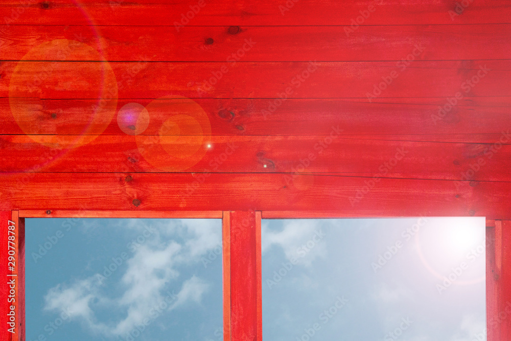 Red wood wall with windows to see blue sky and risen sun. Back light ...