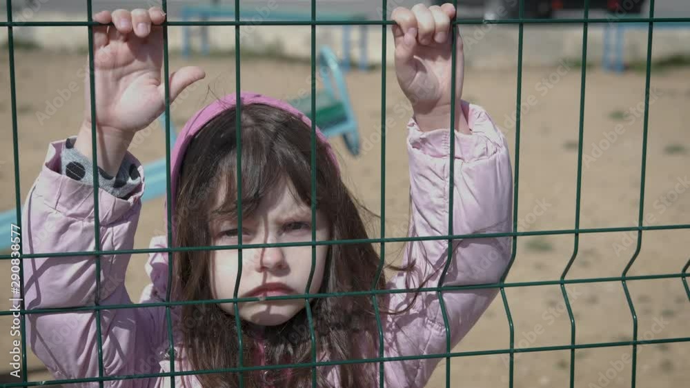 A child behind an iron fence. Loneliness of a child in the playground ...