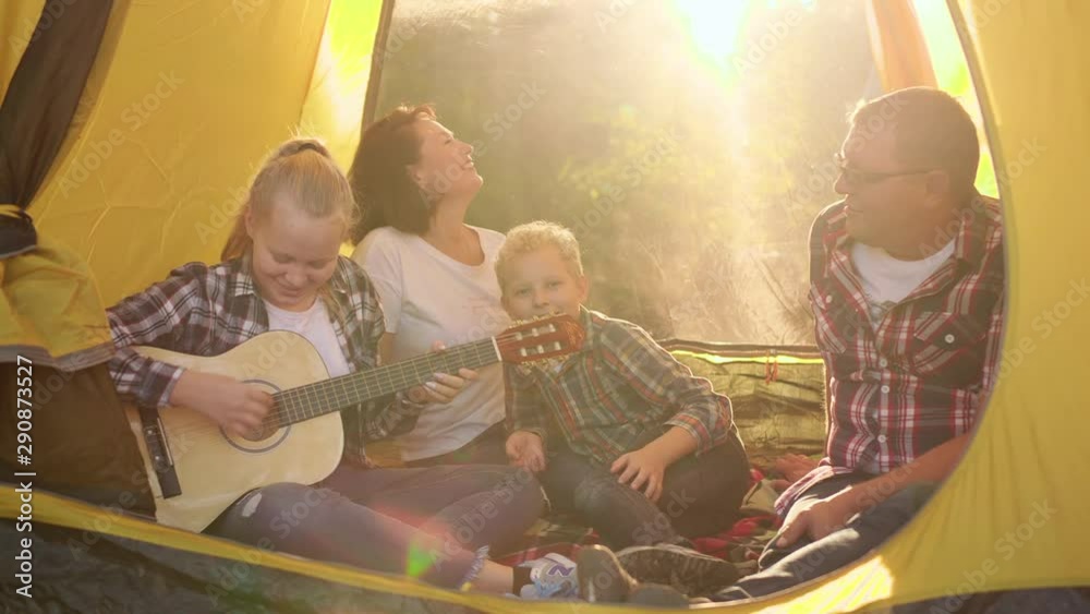 Happy family singing song by guitar in camping tent on sunlight ...