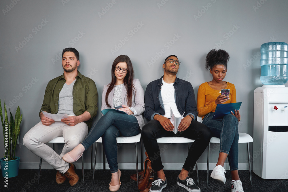 Diverse bored young applicant sitting on chair in row at waiting room ...