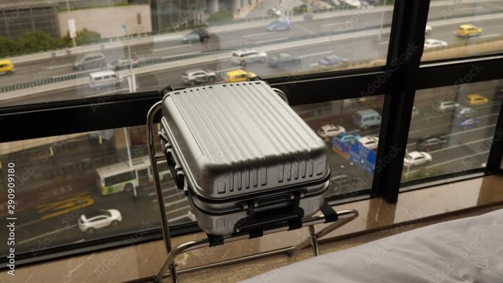 Closed suitcase lie on luggage rack in hotel room against large window ...
