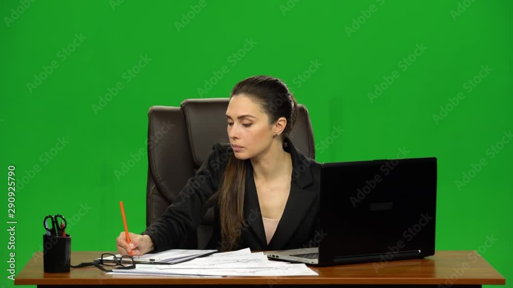 Female manager works on a laptop, think and takes notes. Green screen ...