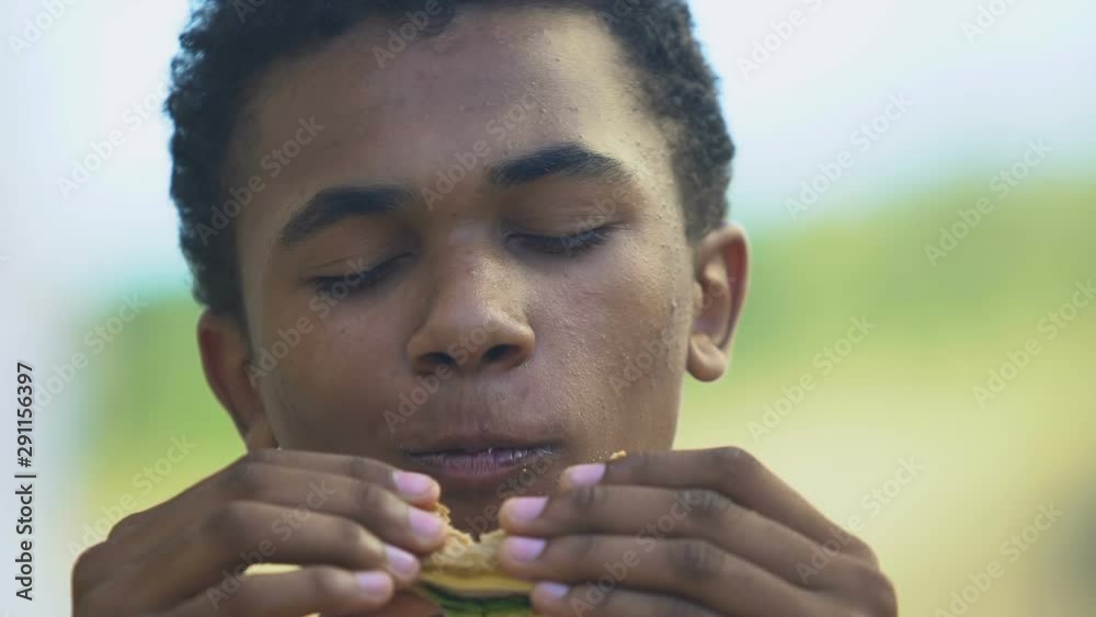 Hungry Afro-American teen boy eating delicious sandwich, lunch brake in ...