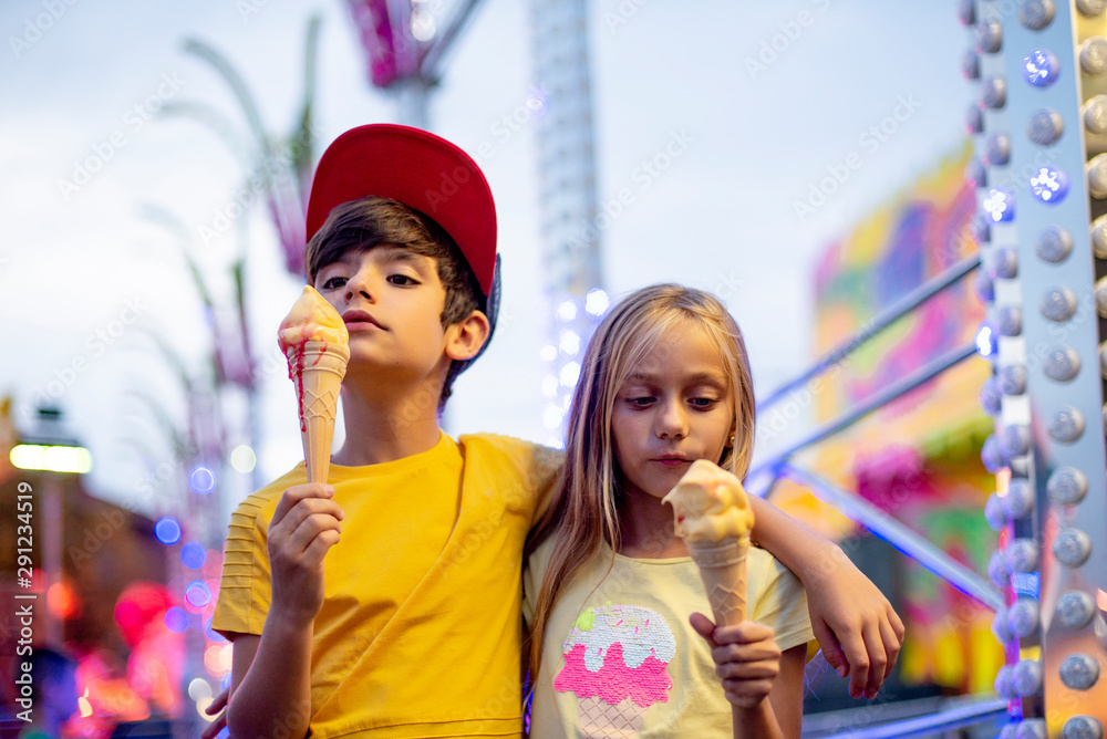 Smiling girl and boy eating ice cream in Funfair Park lights carnival ...