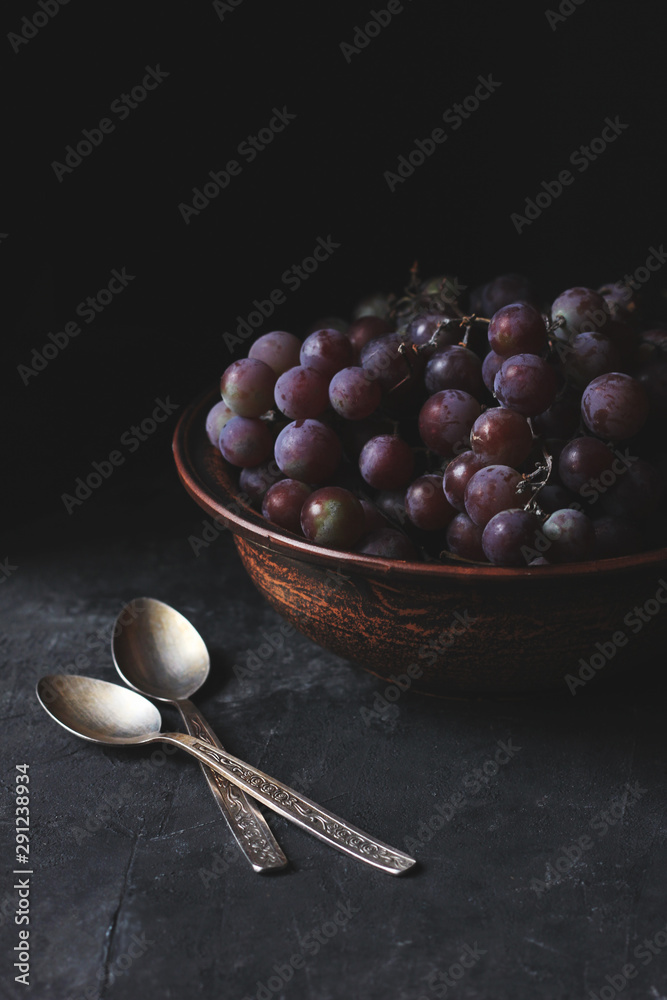 Dark and moody photo of juicy purple grapes in a clay bowl with two ...