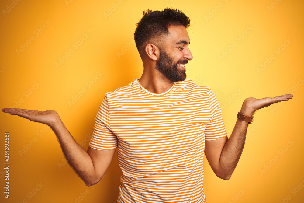 Young indian man wearing t-shirt standing over isolated yellow ...