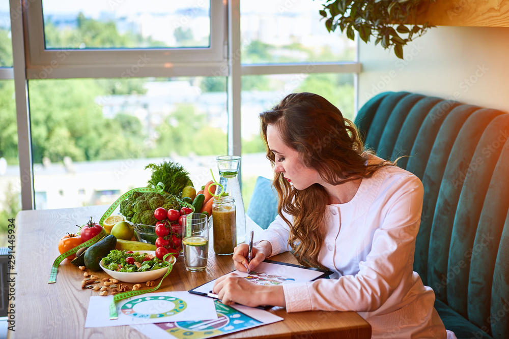Woman dietitian in medical uniform with tape measure working on a diet ...