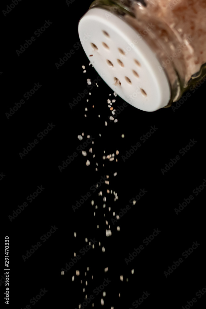 Pink himalayan salt falling out from a salt shaker on a black isolated ...