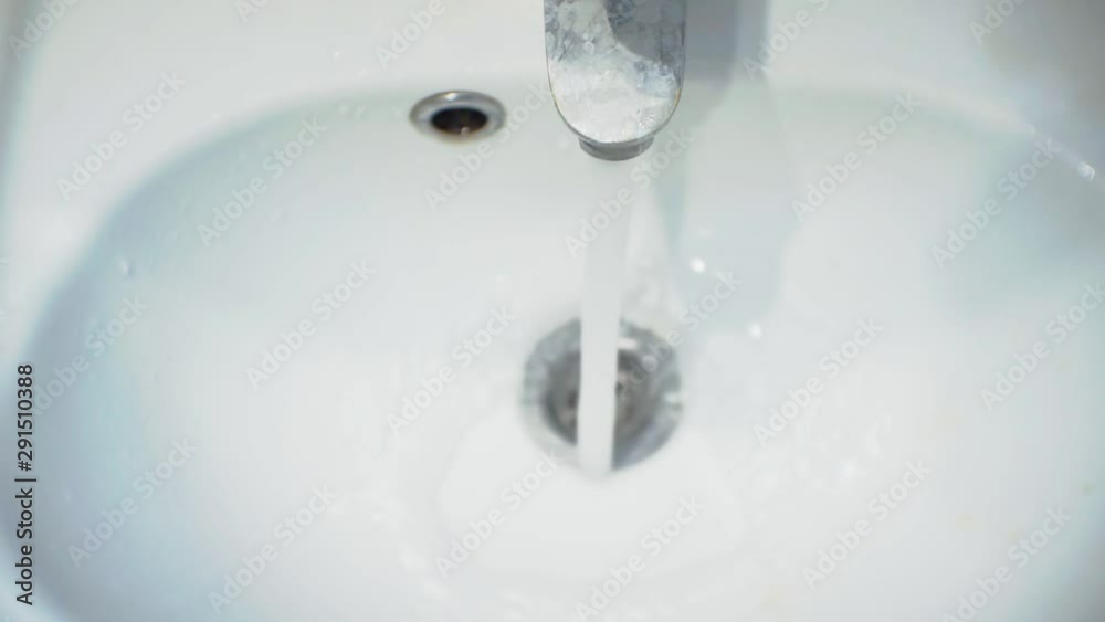 light faience sink with a metal mixer from which a stream of water ...