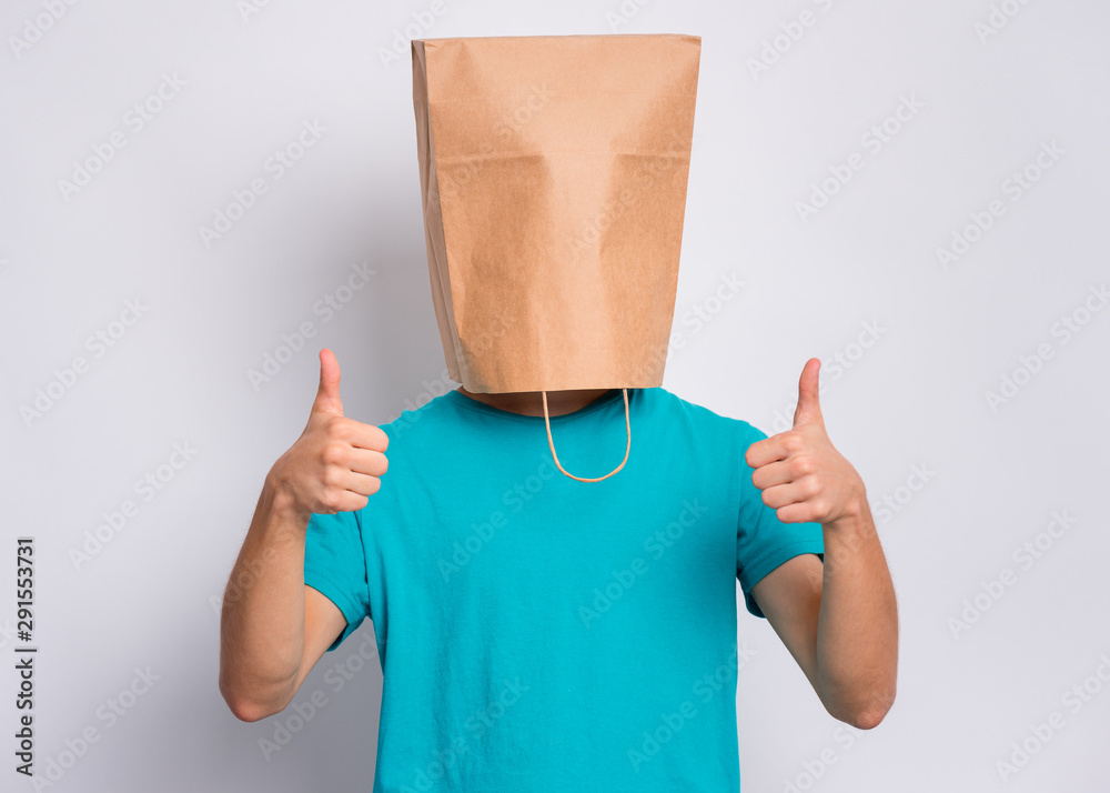 Portrait of teen boy with paper bag over head making thumb up gesture ...