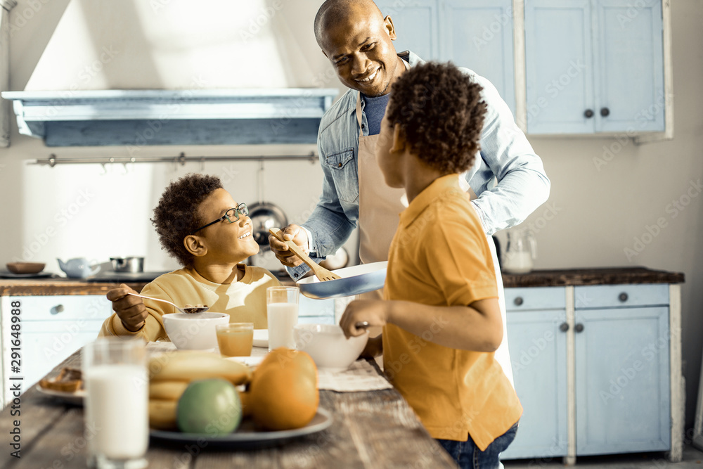 In the sun-drenched kitchen a man and his two sons eating and chatting ...