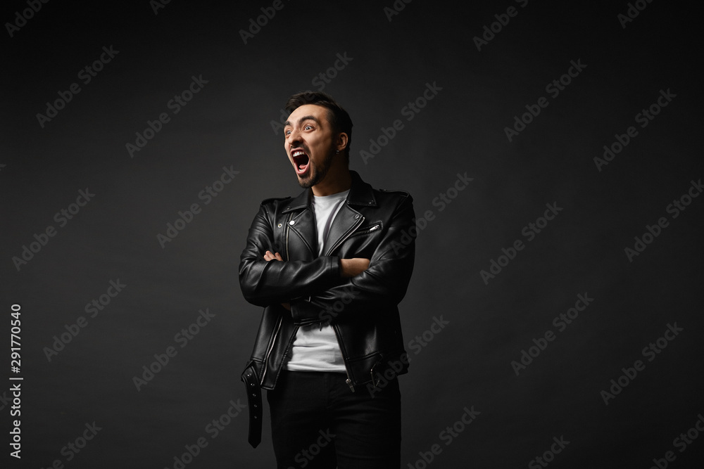 Screaming brutal handsome man in black leather jacket folded one's arms ...