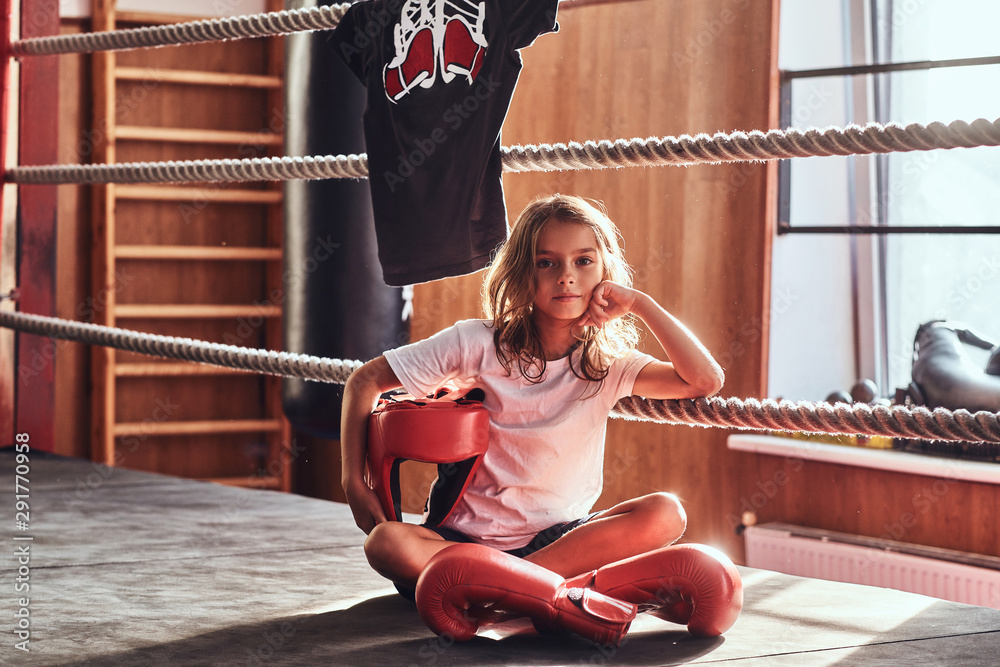 Beautiful kid girl is sitting on boxing ring wearing boxer uniform ...