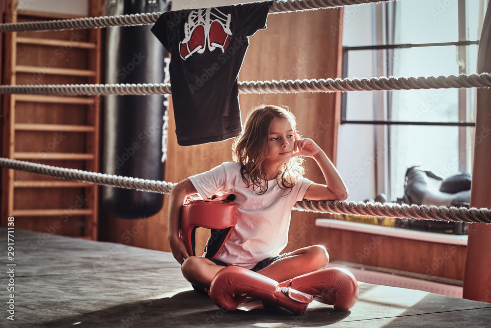 Beautiful kid girl is sitting on boxing ring wearing boxer uniform ...