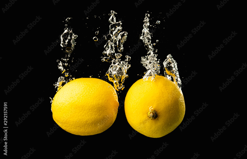 Fresh yellow lemons in water splash on black background with lots of ...