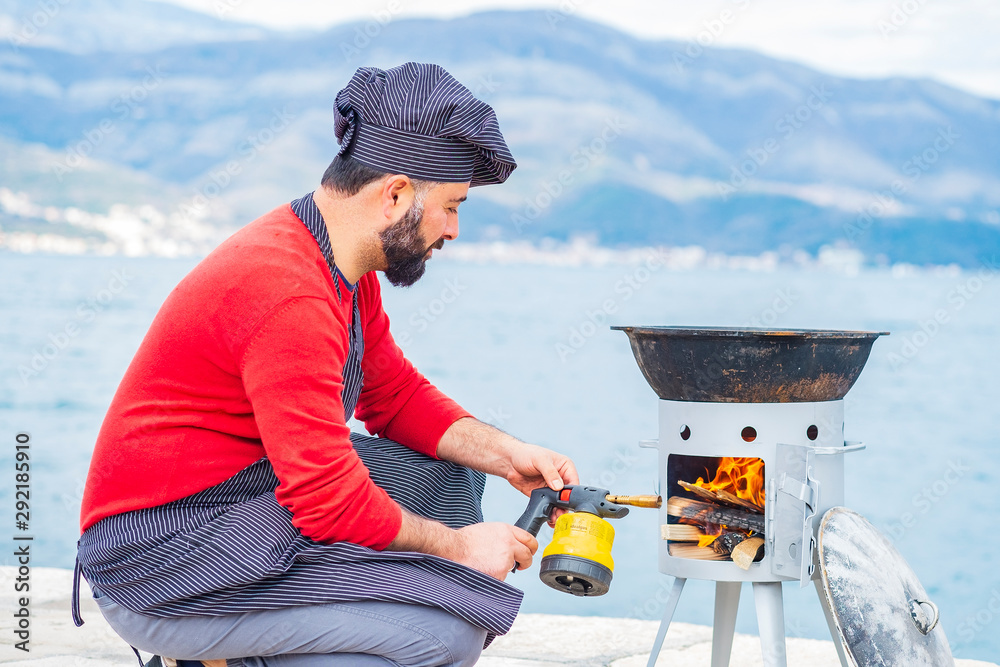 Caucasian man makes a fire under a cauldron for a pilaf with a gas ...