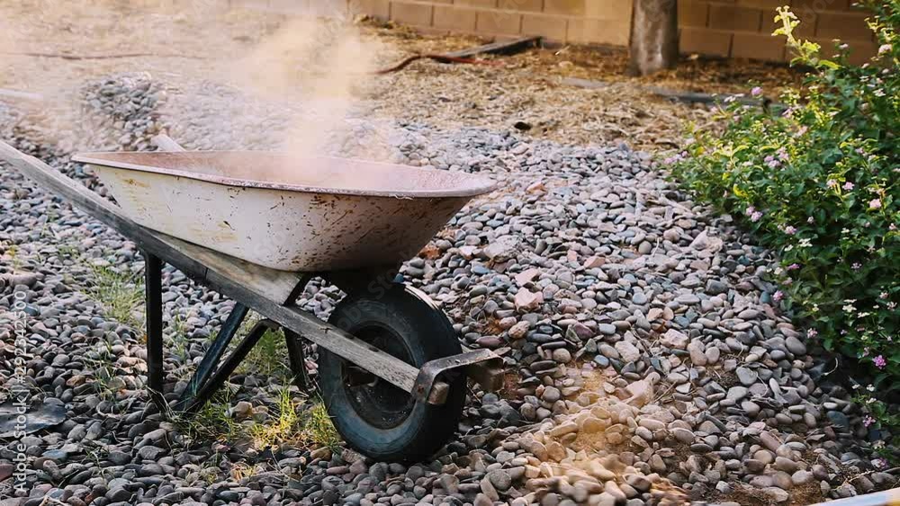 Full view of wheelbarrow as river rock is being shoveled into it ...