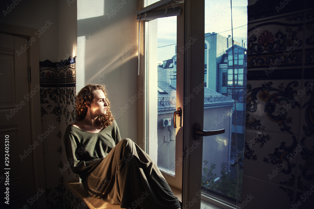 Beautiful young sad girl is sitting by the window Stock Photo | Adobe Stock