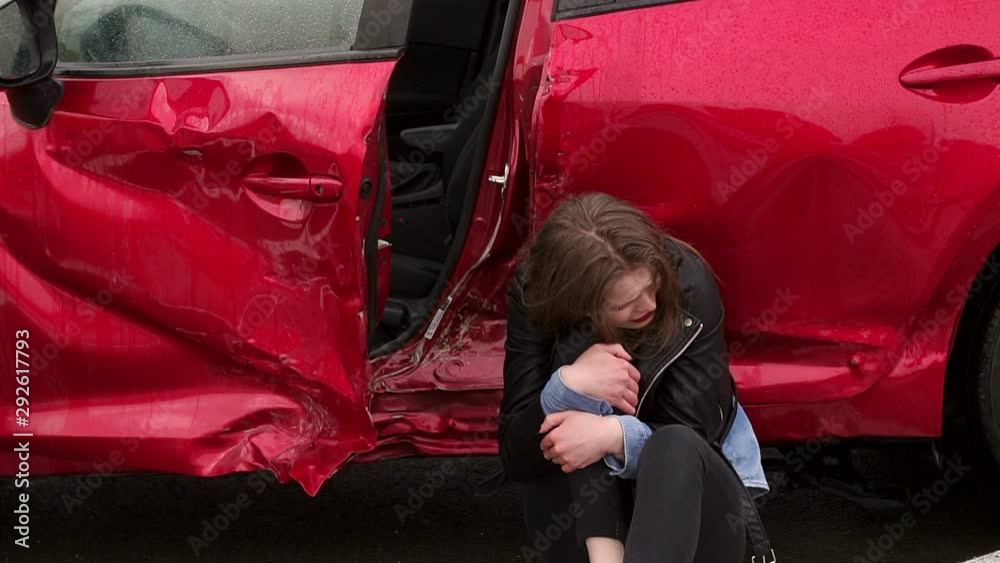 Close-up of a young girl sitting leaning against her broken car after a ...