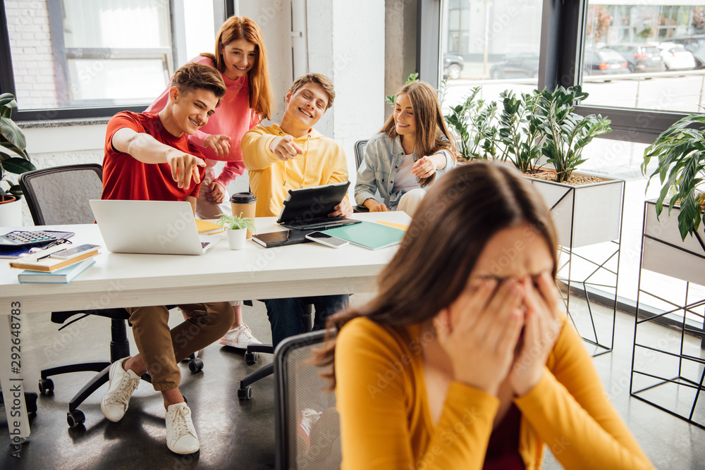 schoolchildren laughing while bullying sad girl on foreground Stock ...