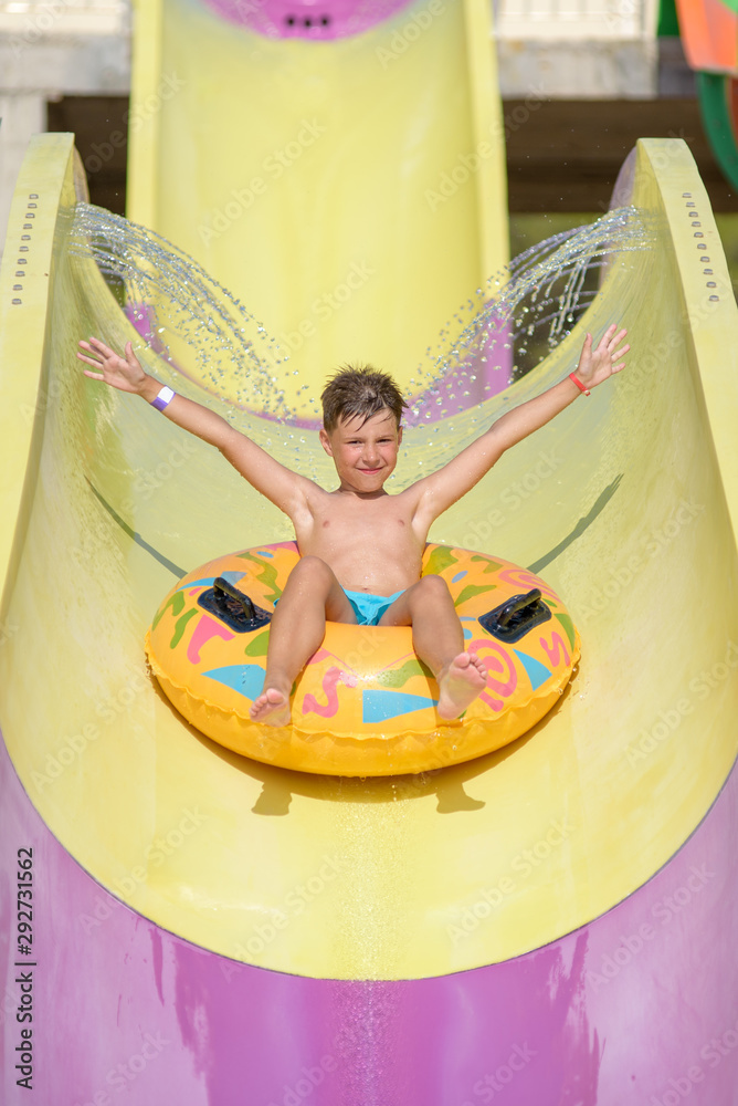 Portrait of happy boy on water slide in swimming pool having fun during ...