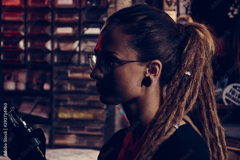 Dark portrait of attractive young female tattoo master at her own salon ...