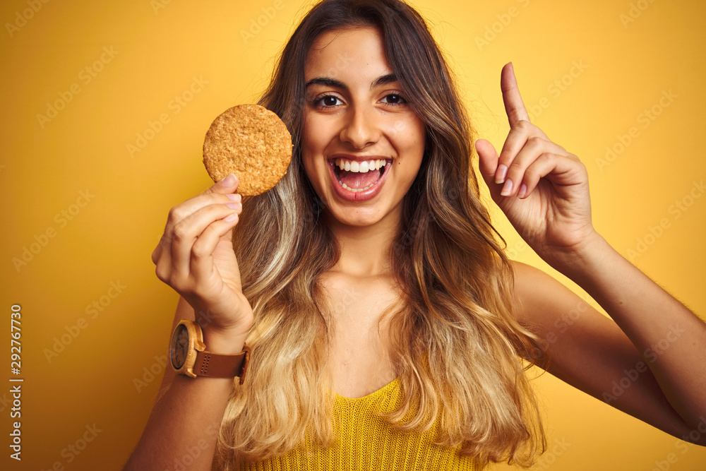 Young beautiful woman eating biscuit over grey isolated background ...