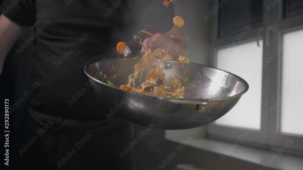 Chef tosses fried vegetables with noodles in hot wok in slow motion ...