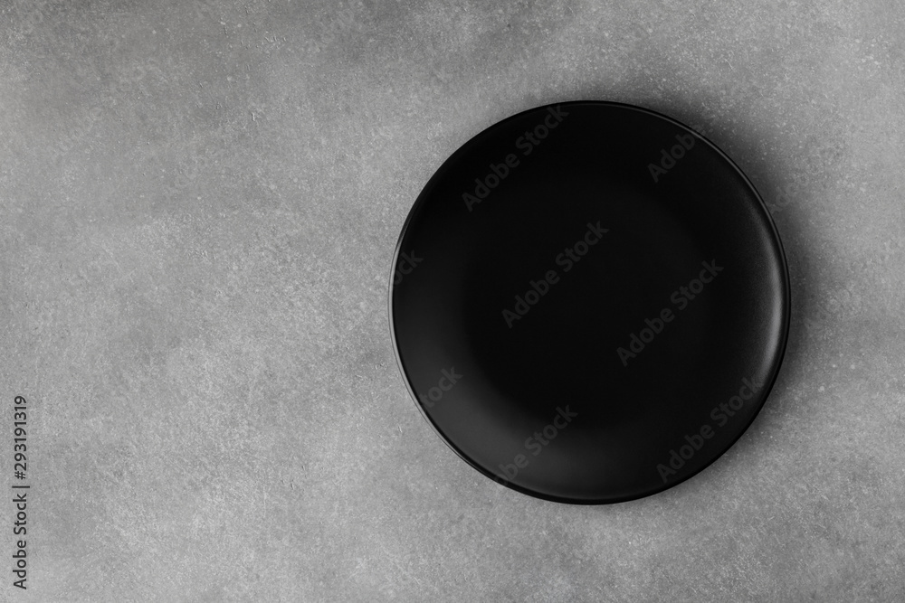 Black plate on gray stone table top view. Empty space for menu or ...