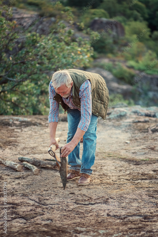 Old man with gray hair and beard chopping woods for campfire in canyon ...