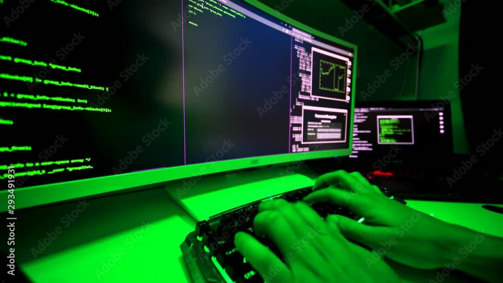 Hacker's hands on keyboard typing malicious code on large screen. A black-hat programmer hacking ...