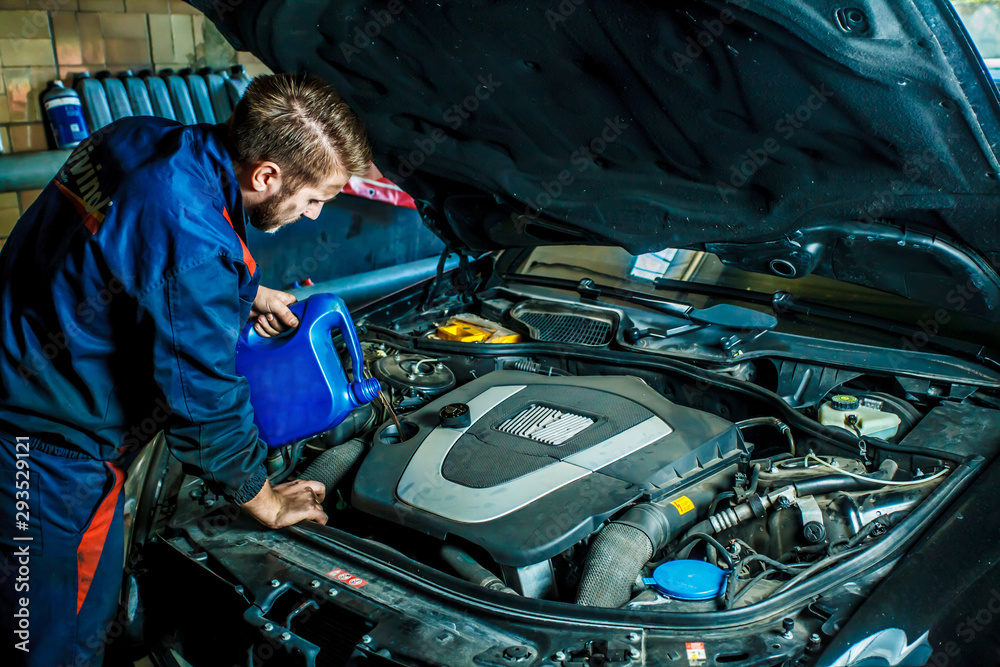 Car mechanic replacing and pouring oil into engine at maintenance ...