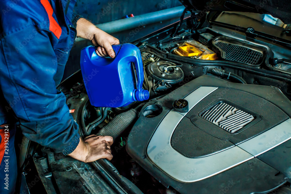 Car mechanic replacing and pouring oil into engine at maintenance ...