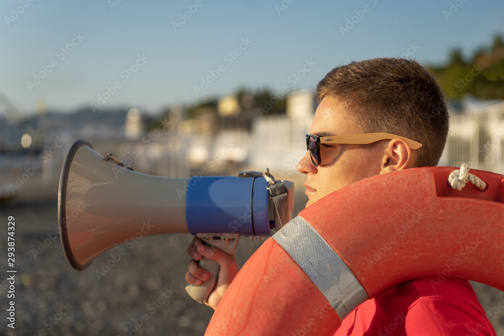 Young lifeguard with megaphone on beach background. Lifeguard on duty ...