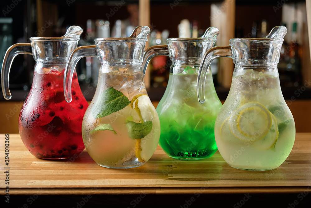 Different soft drinks in transparent jugs on a dark wooden background ...
