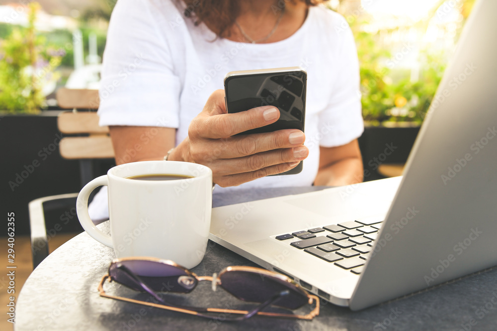 Woman working with laptop and smartphone sitting outdoor in a beautiful ...