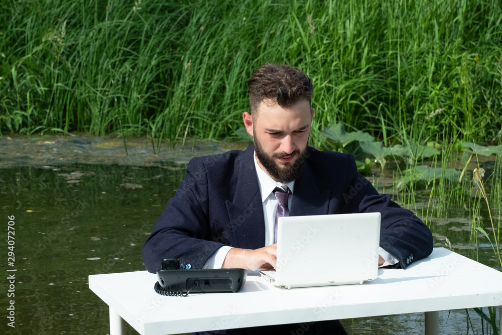 Office in the swamp. A young businessman with a beard in a suit as a ...