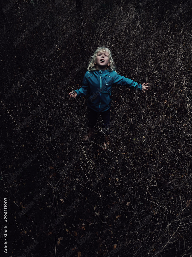 Little blonde Caucasian scared girl lost in wood forest looking up ...