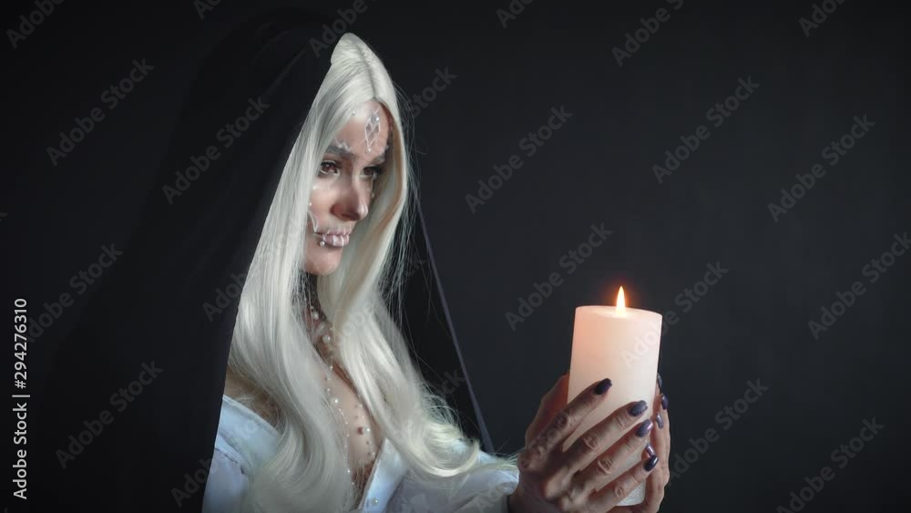 evil witch with long white hair and black hood on head holds candle in ...