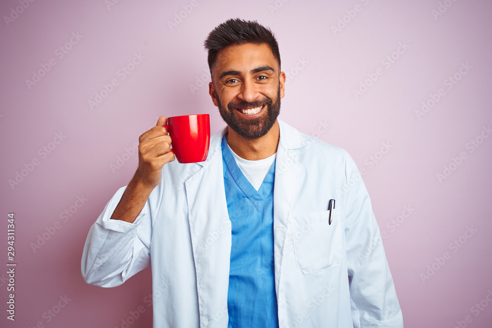 Young indian doctor man drinking cup of coffee standing over isolated ...