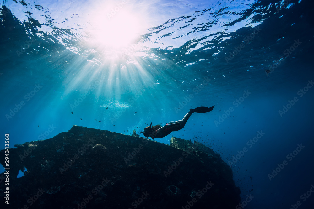 Free diver girl in pink swimwear with fins swimming underwater at wreck ...