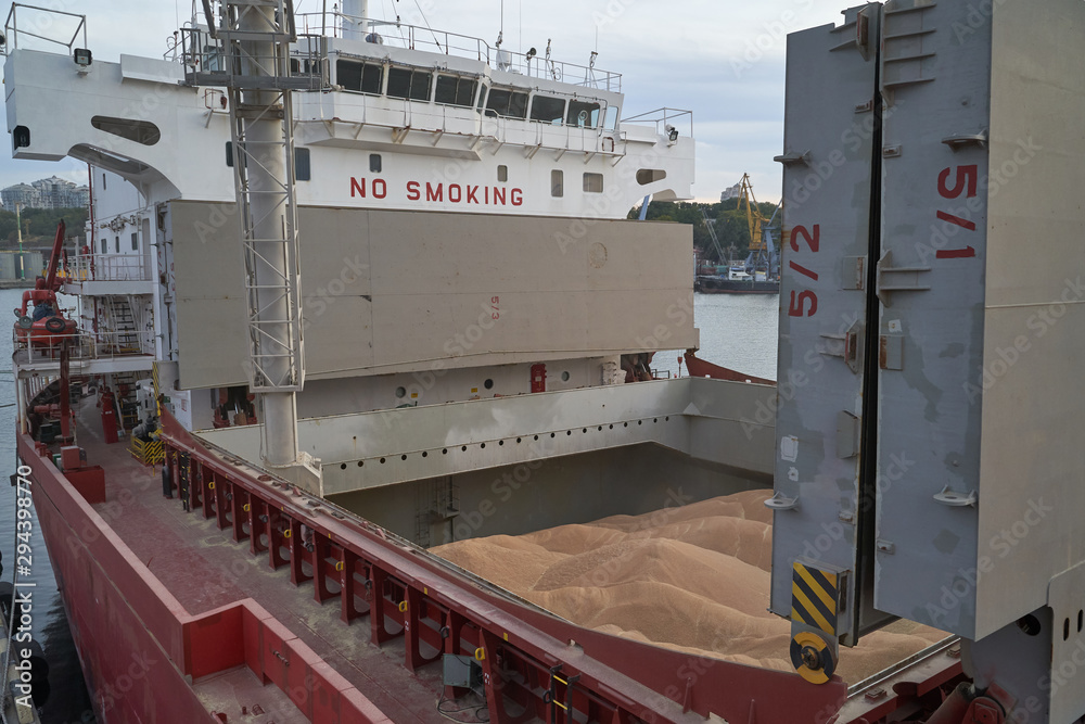 Grain loading in hold of bulk carrier ship with elevator crane closeup ...