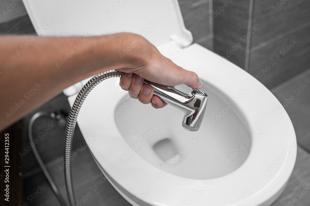 Using of bidet shower with a white toilet. Bidet shower in male hand ...