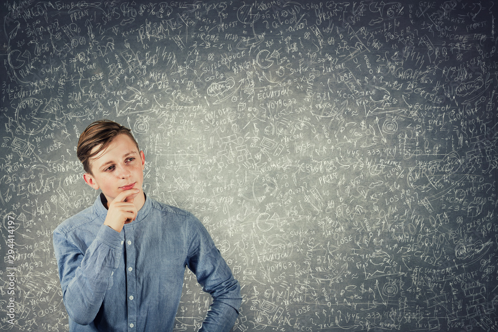 Smart teenage boy thinking, keeps hand under chin, stands in front of a ...