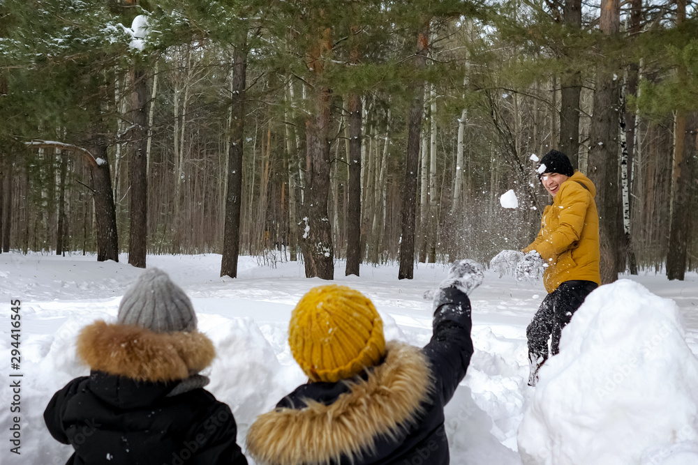 Man is playing snowballs with his family in winter park. His wife and ...